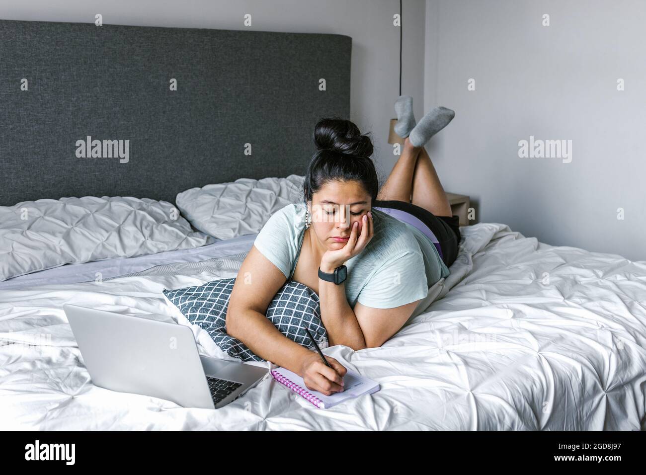 Young latin plus size woman lying in bed taking notes in notebook using ...