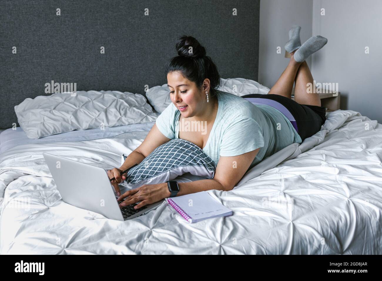 Curvy latin woman lying on bed using computer in Latin America, plus ...