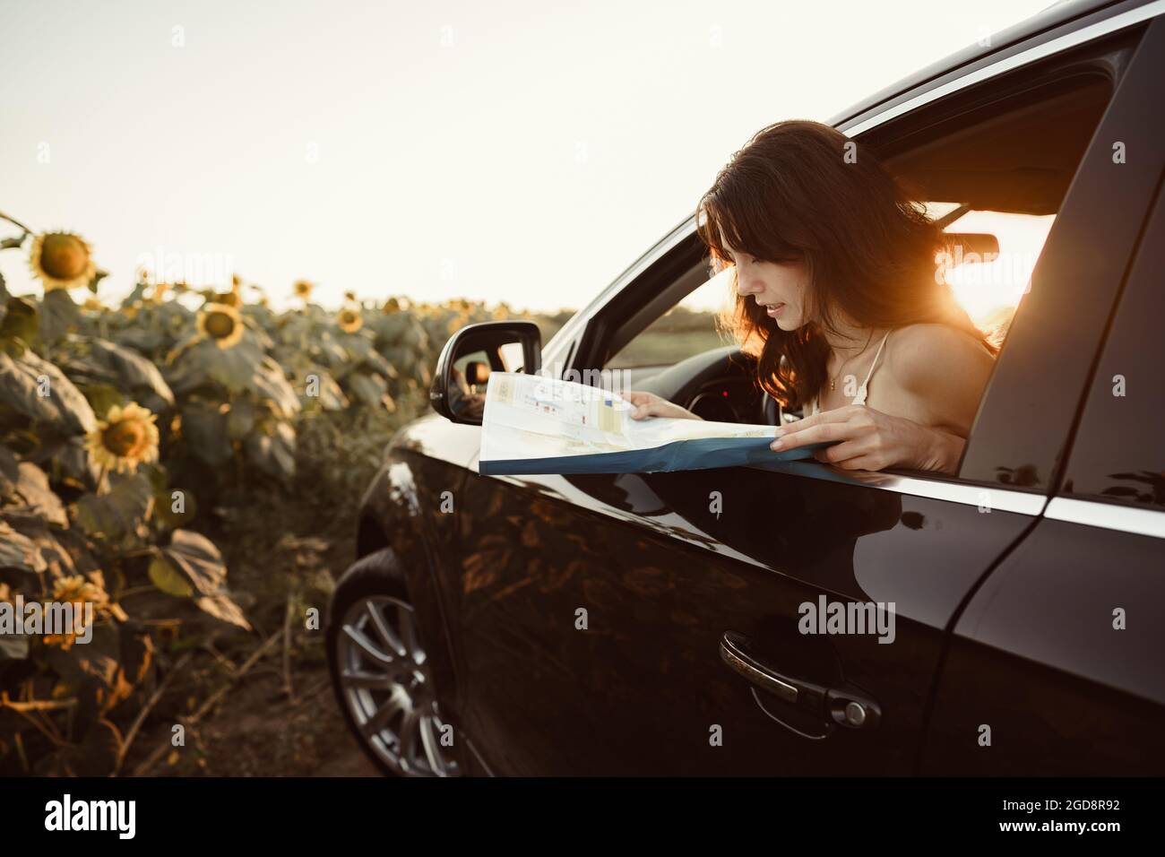Lost young woman sitting in her car in the countryside and looking at ...