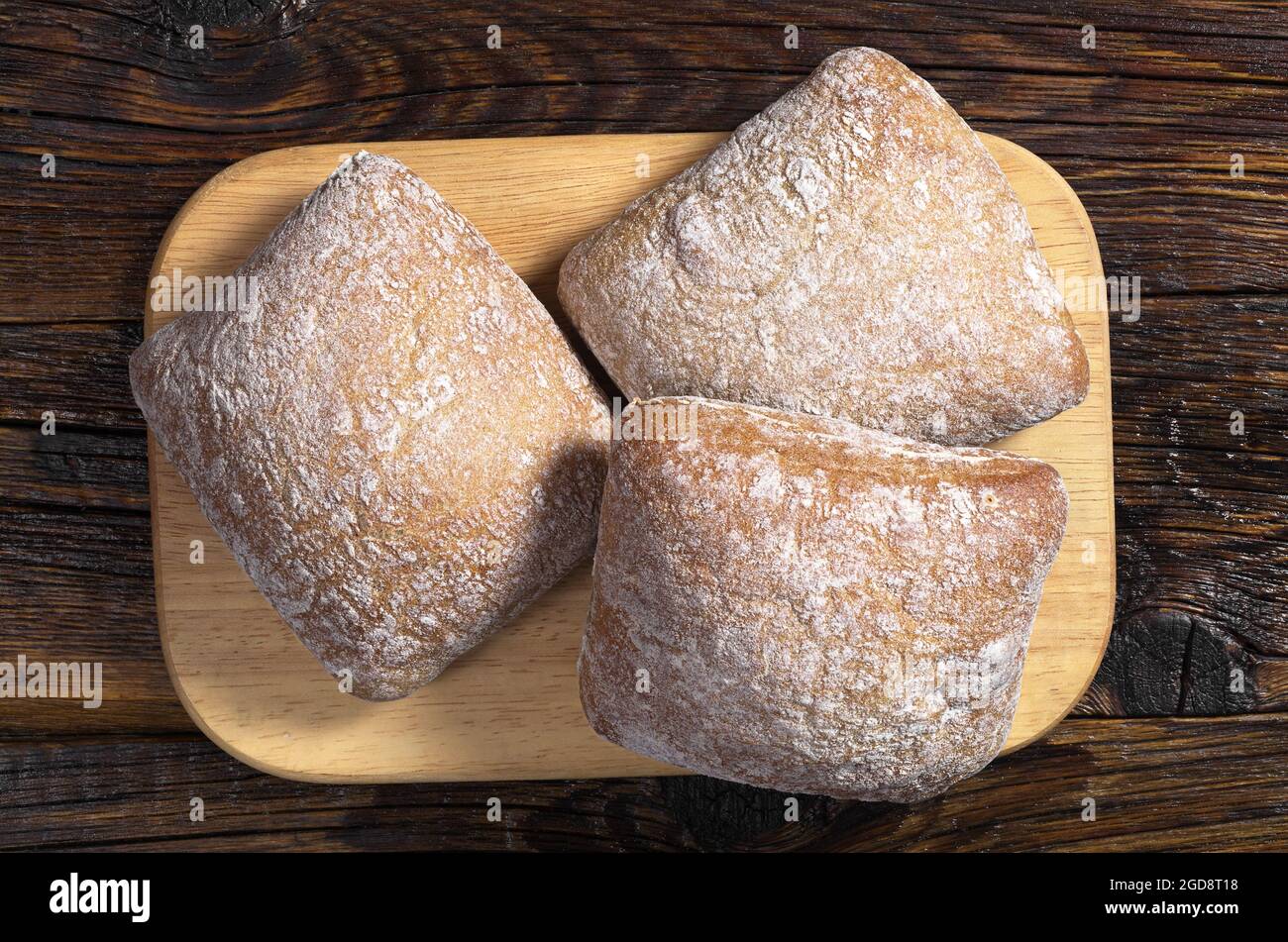 Small loaves of bread ciabatta on cutting board on dark wooden table ...