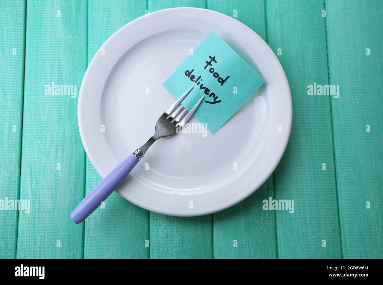 Note paper with message attached to fork, on plate, on color wooden ...