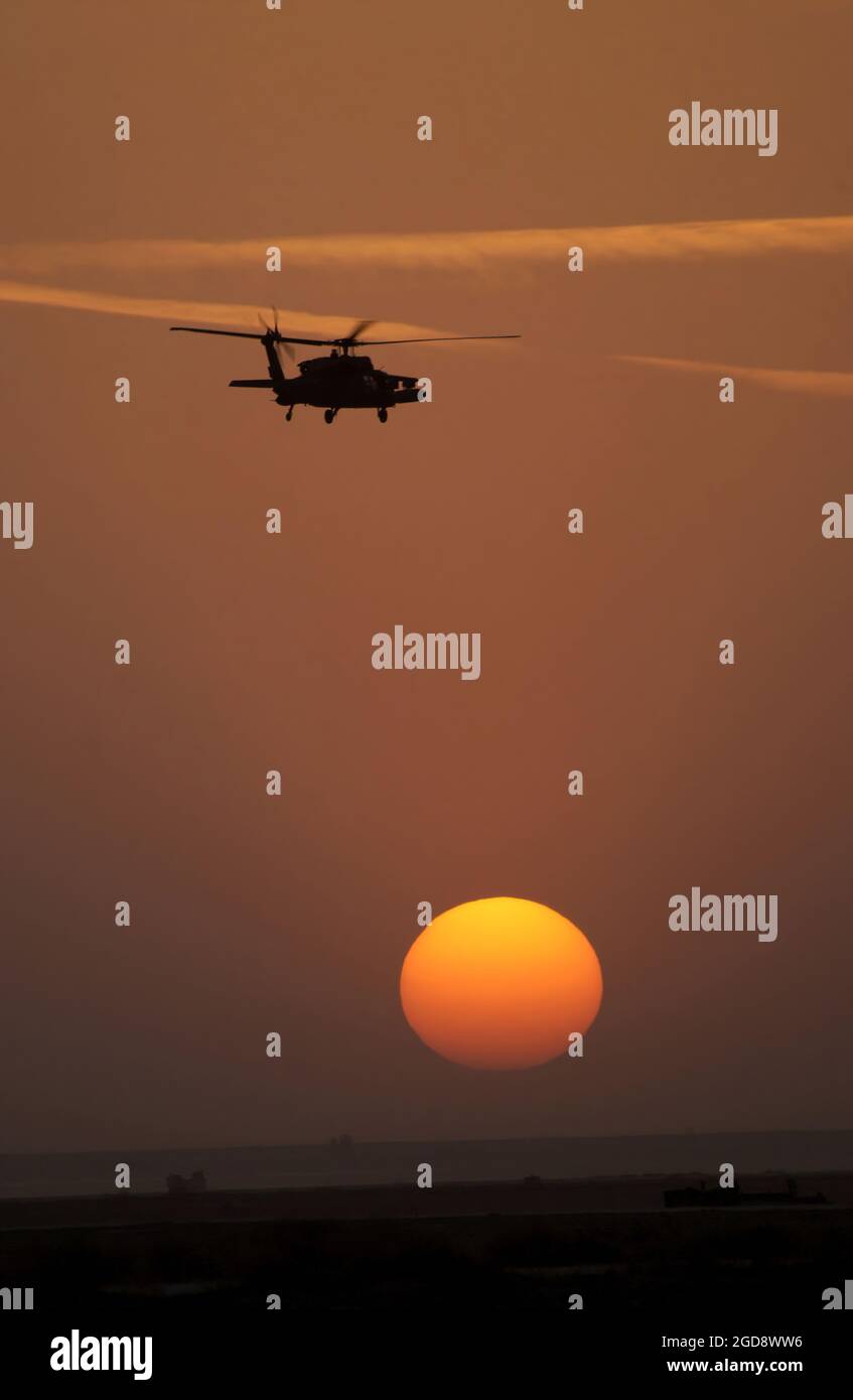 A US Army HH-60G Pave Hawk helicopter flies past an orange setting sun ...