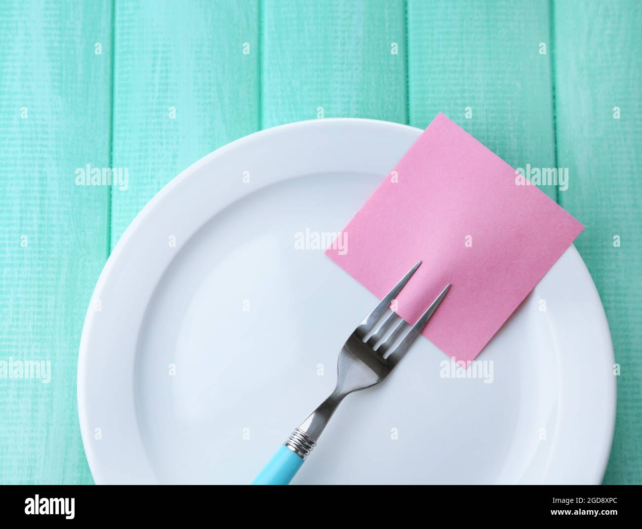 Empty note paper attached to fork, on plate, on color wooden background ...