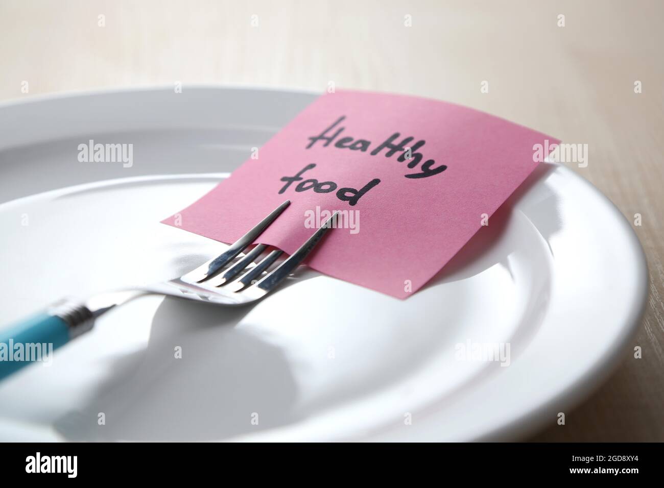 Note paper with message attached to fork, on plate, on color wooden ...