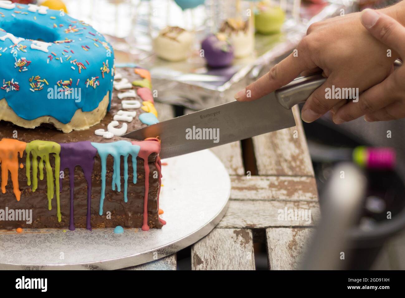 A colorful two-layer cake being cut, featuring vibrant icing drips and ...