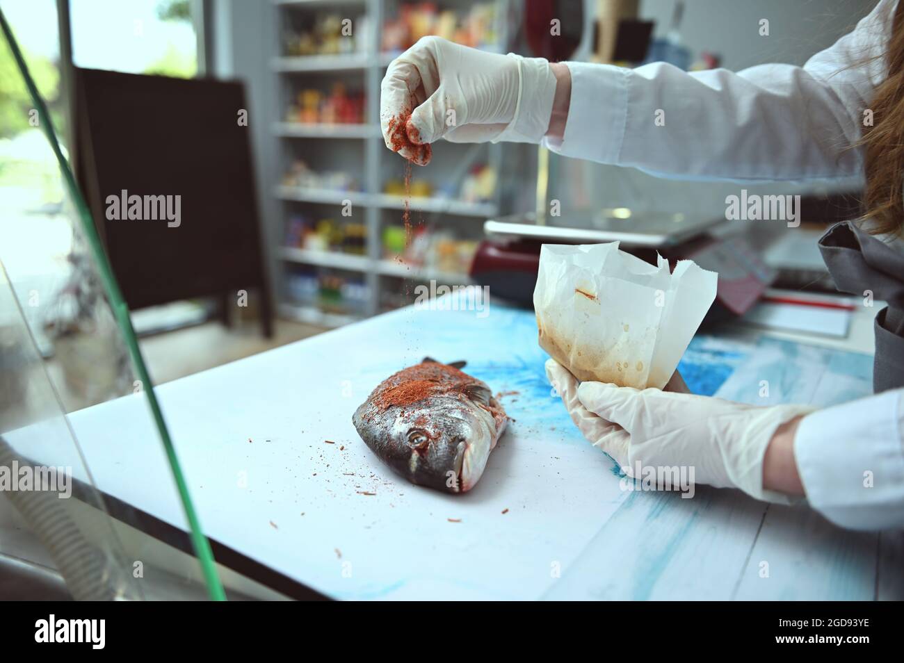 Fishmonger gloved hand sprinkling seasonings on a cooldes dorado fish ...