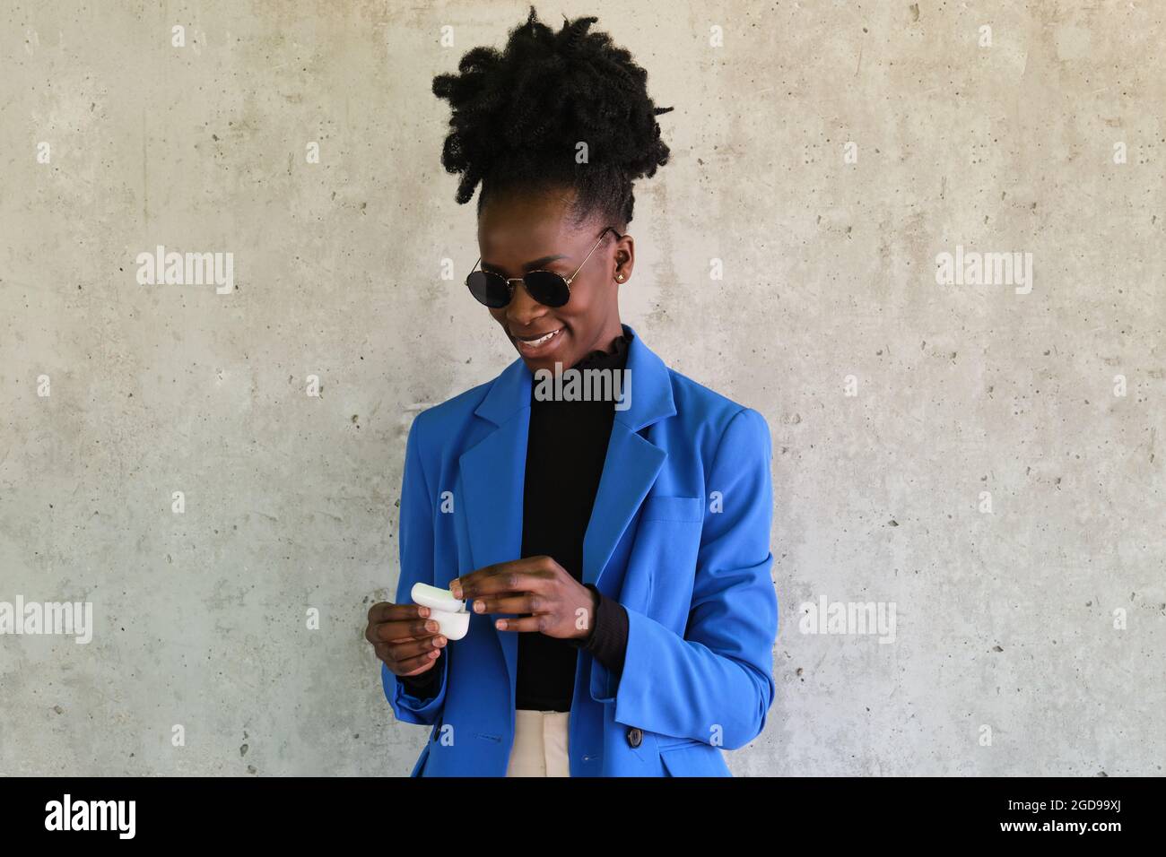 African woman putting on wireless earbuds, with blue jacket suit and ...