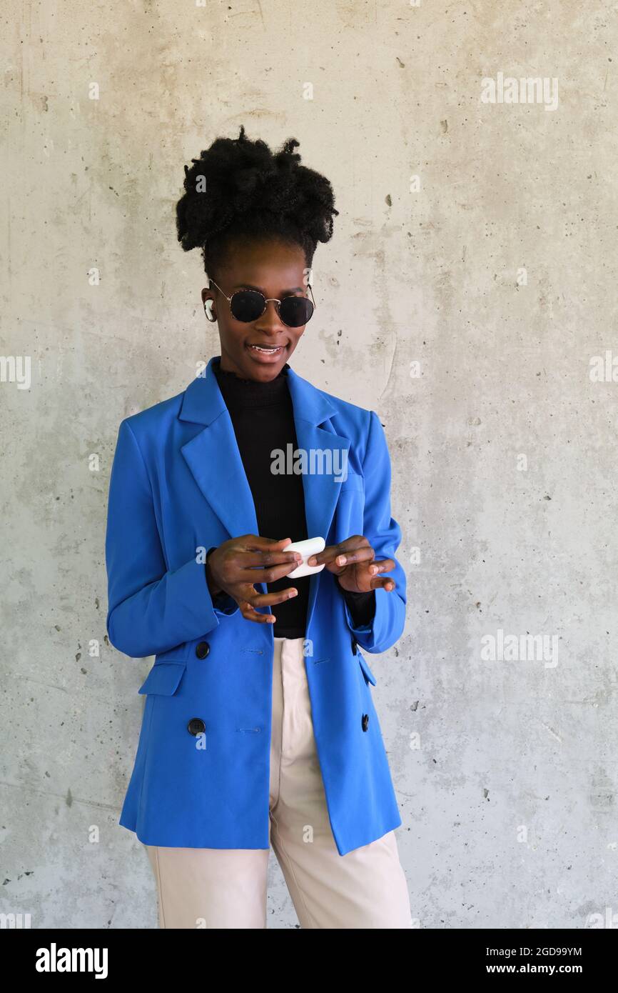 African woman putting on wireless earbuds, with blue jacket suit and ...