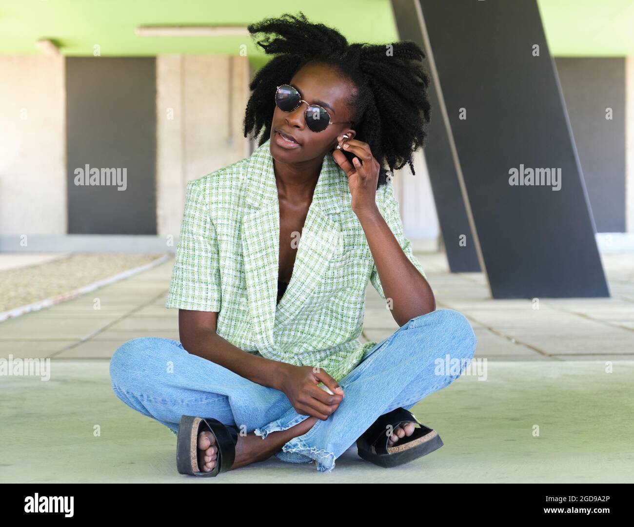 African woman putting on wireless earbuds with green jacket suit and ...