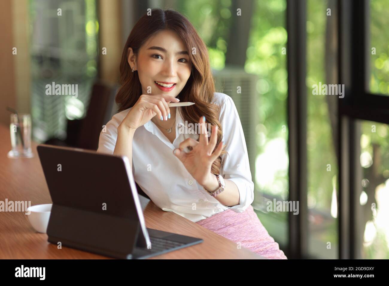 Happy businesswoman showing ok hand sign while sitting at work place ...