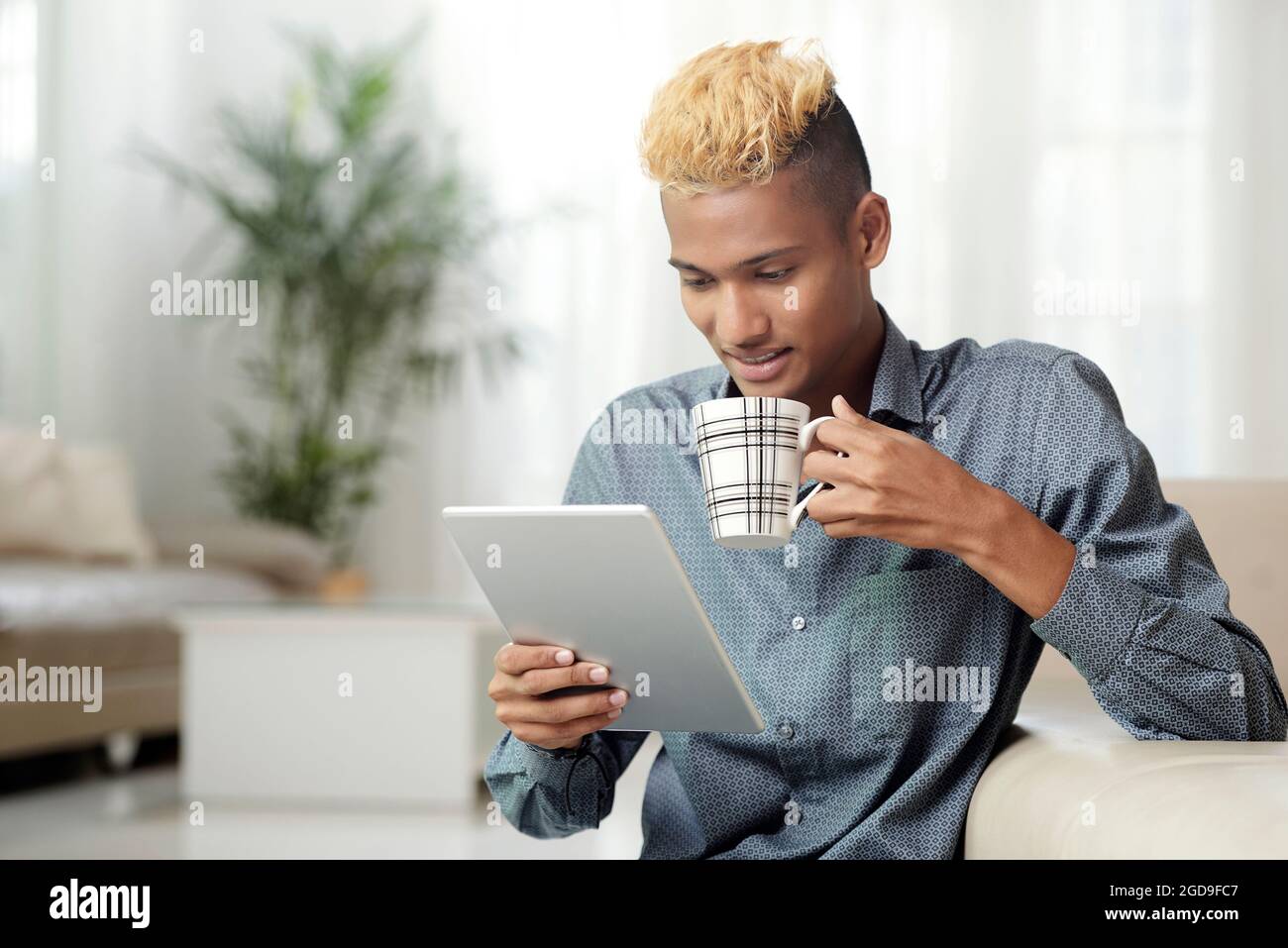 Positive handsome young man with digital tablet drinking morning coffee ...