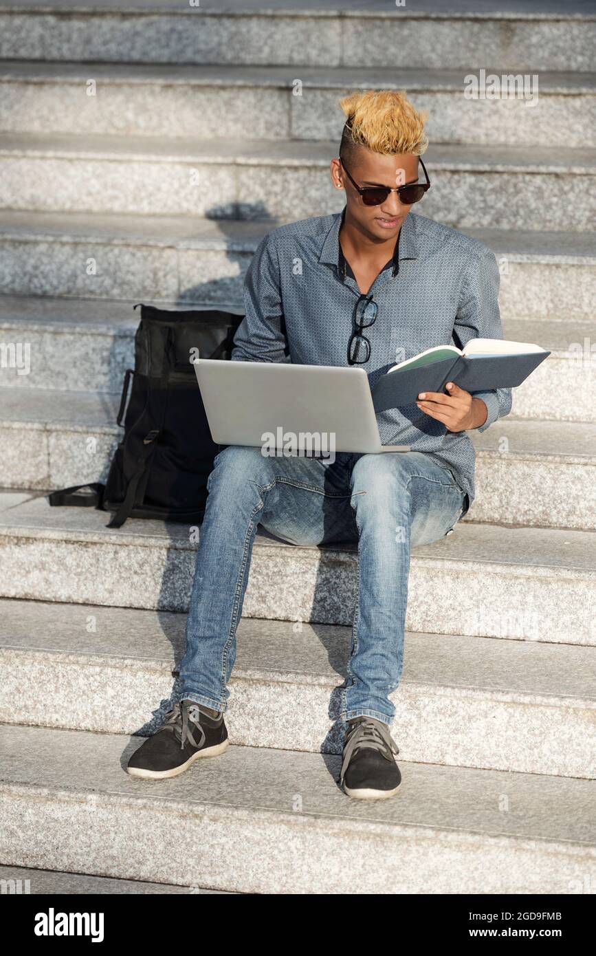 Computer science student sitting on steps of college building, reading ...