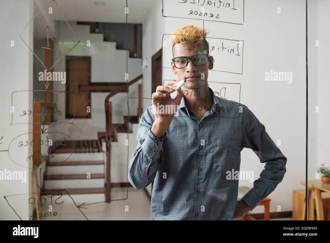 Serious young software developer drawing general flow chart on glass ...