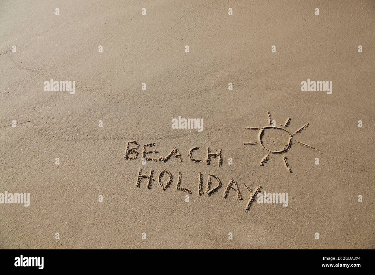 Beach Holiday written in the sand with a sun symbol Stock Photo - Alamy