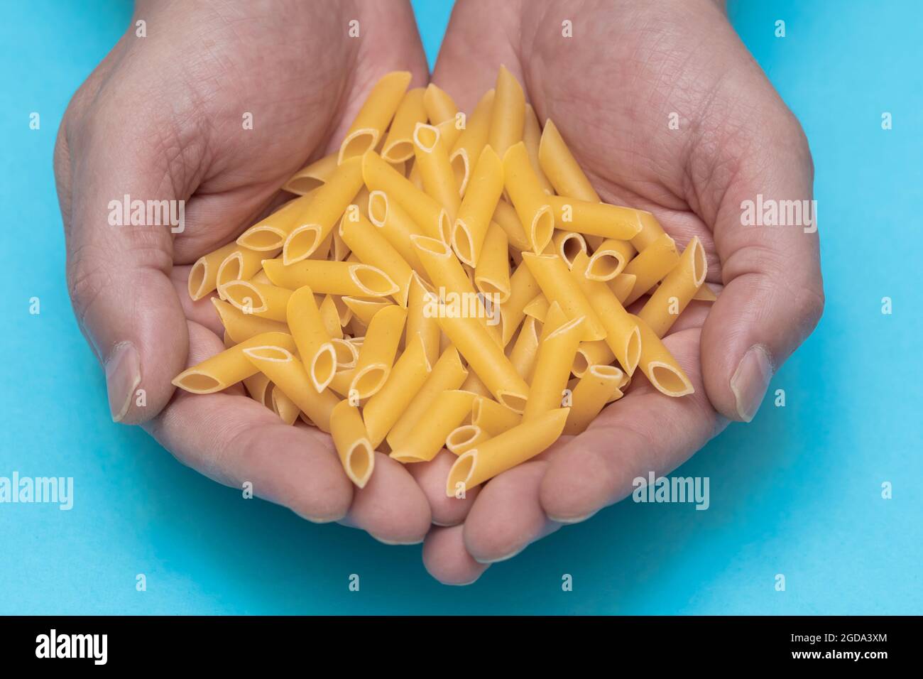 A person's hands holding a handful of macaroni on blue background ...