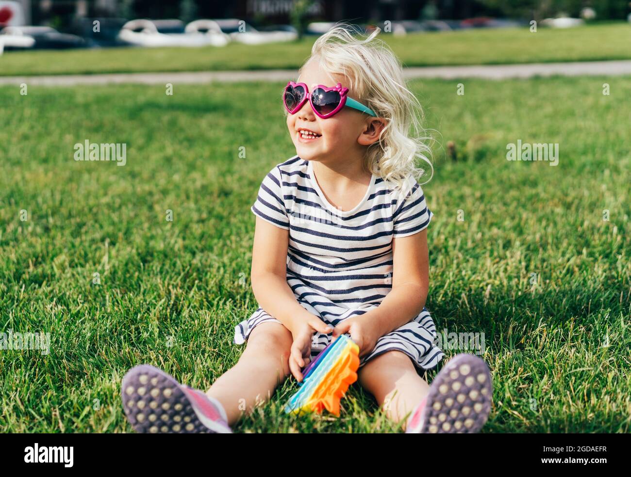 Cheerful emotional laughing little blonde girl is sitting on the lawn ...