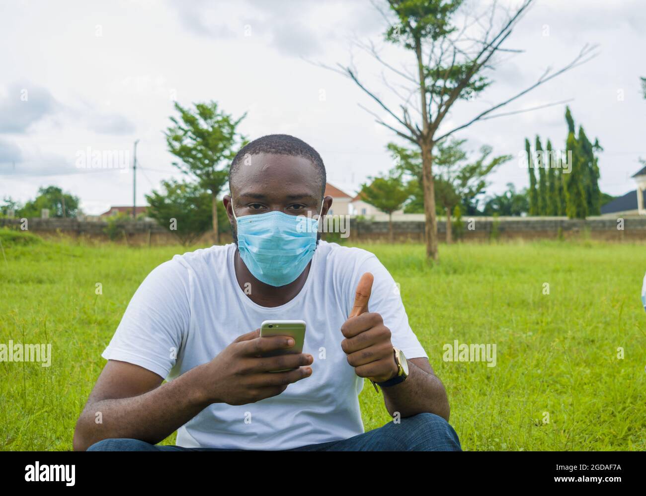 Closeup of an African man sitting on the grass and wearing a face mask ...
