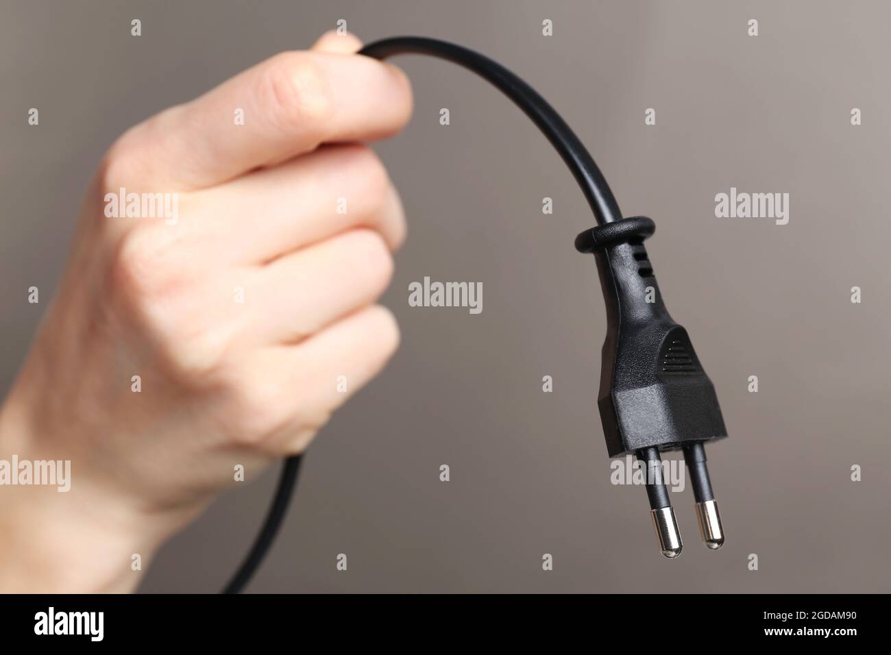 Hand holding electric plug on grey background Stock Photo - Alamy