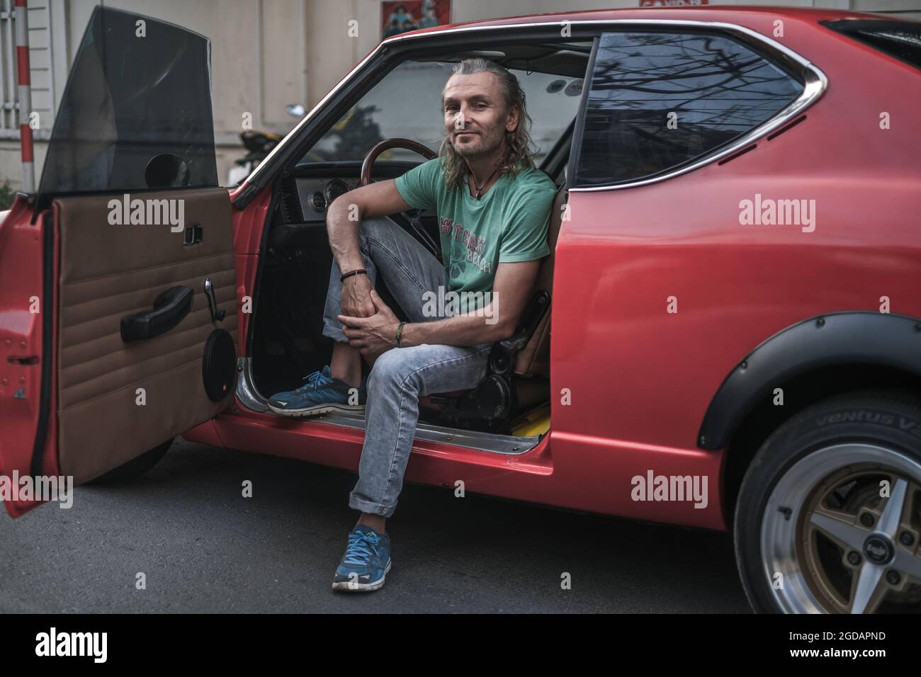 Mature handsome man sitting in red old style car and looking at camera ...