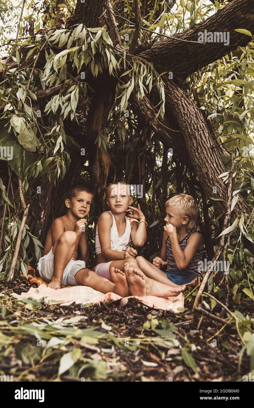 Three children play in a hut which they themselves have built from ...