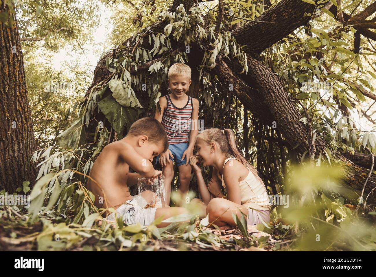Three children play in a hut which they themselves have built from ...