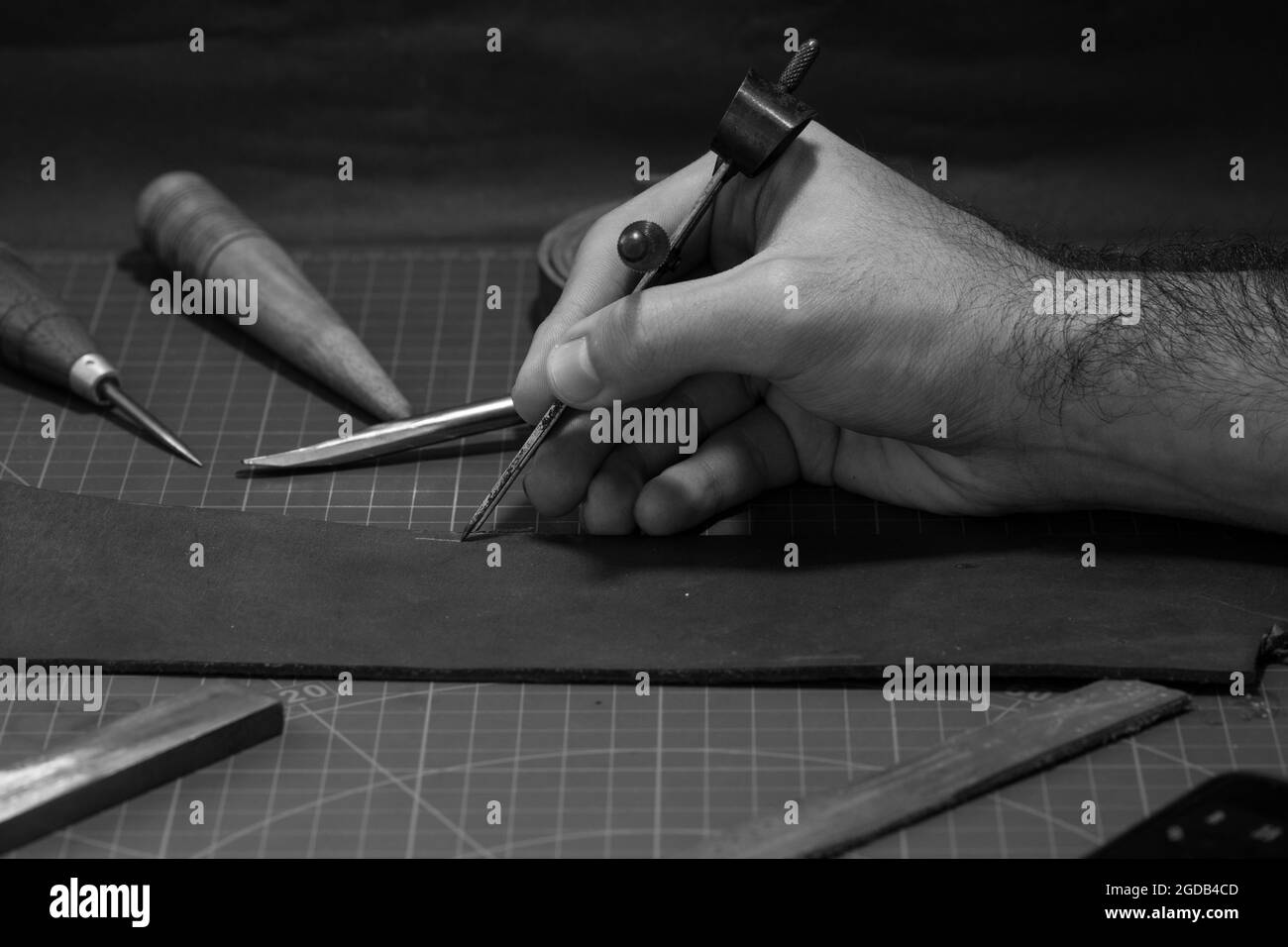 Grayscale closeup of a man's hand working with a tool for leather ...