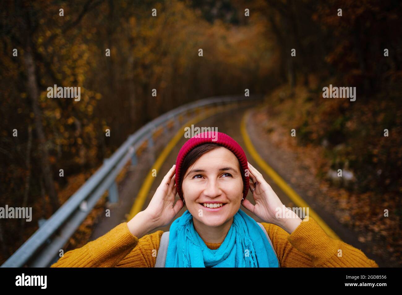 beautiful female hipster in a red hat, yellow sweater and blue scarf walks in the autumn nature ...