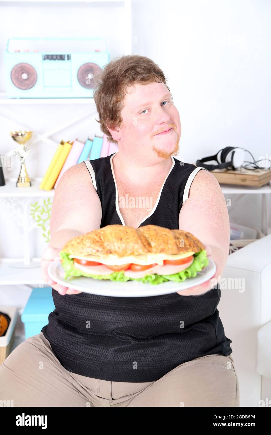 Fat man eating tasty sandwich on home interior background Stock Photo ...