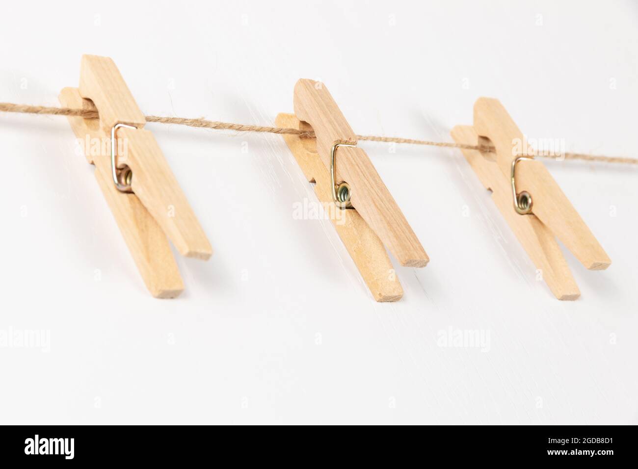 three wooden clothespins with a metal spring hang on a rope on a white ...