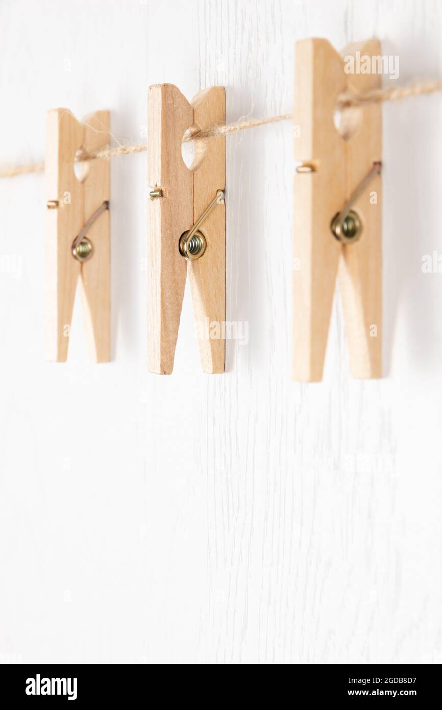 three wooden clothespins with a metal spring hang on a rope on a white ...