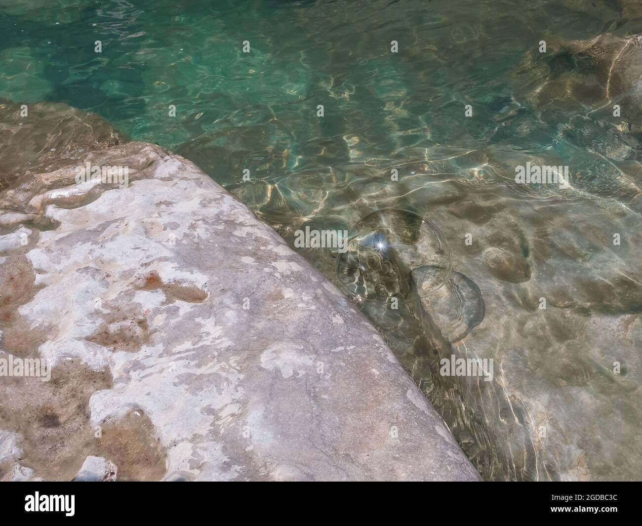 A shiny soap bubble floats on transparent river with a rocky bottom ...