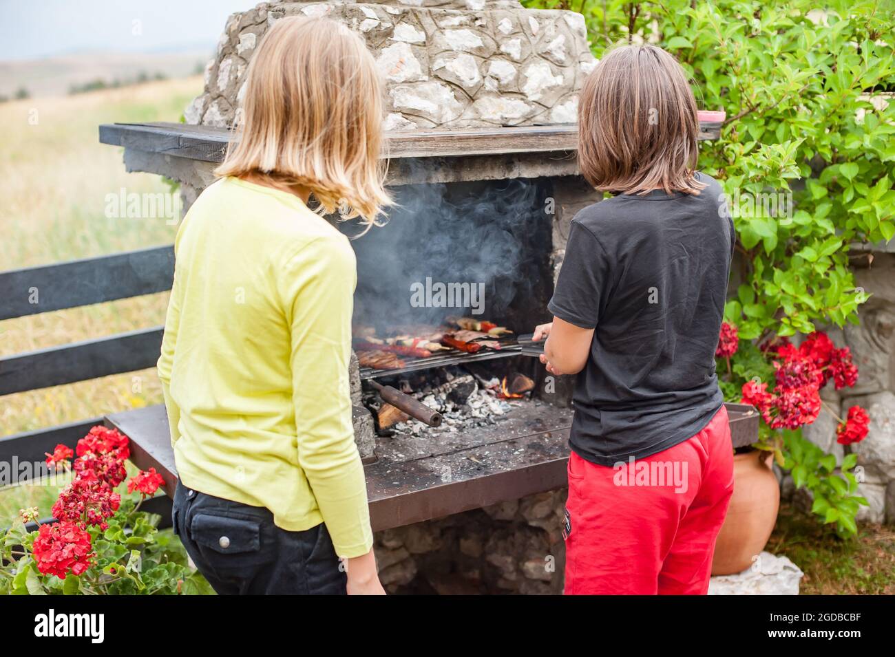 Children grilling meat. Boy and girl making barbecue on the grill on ...
