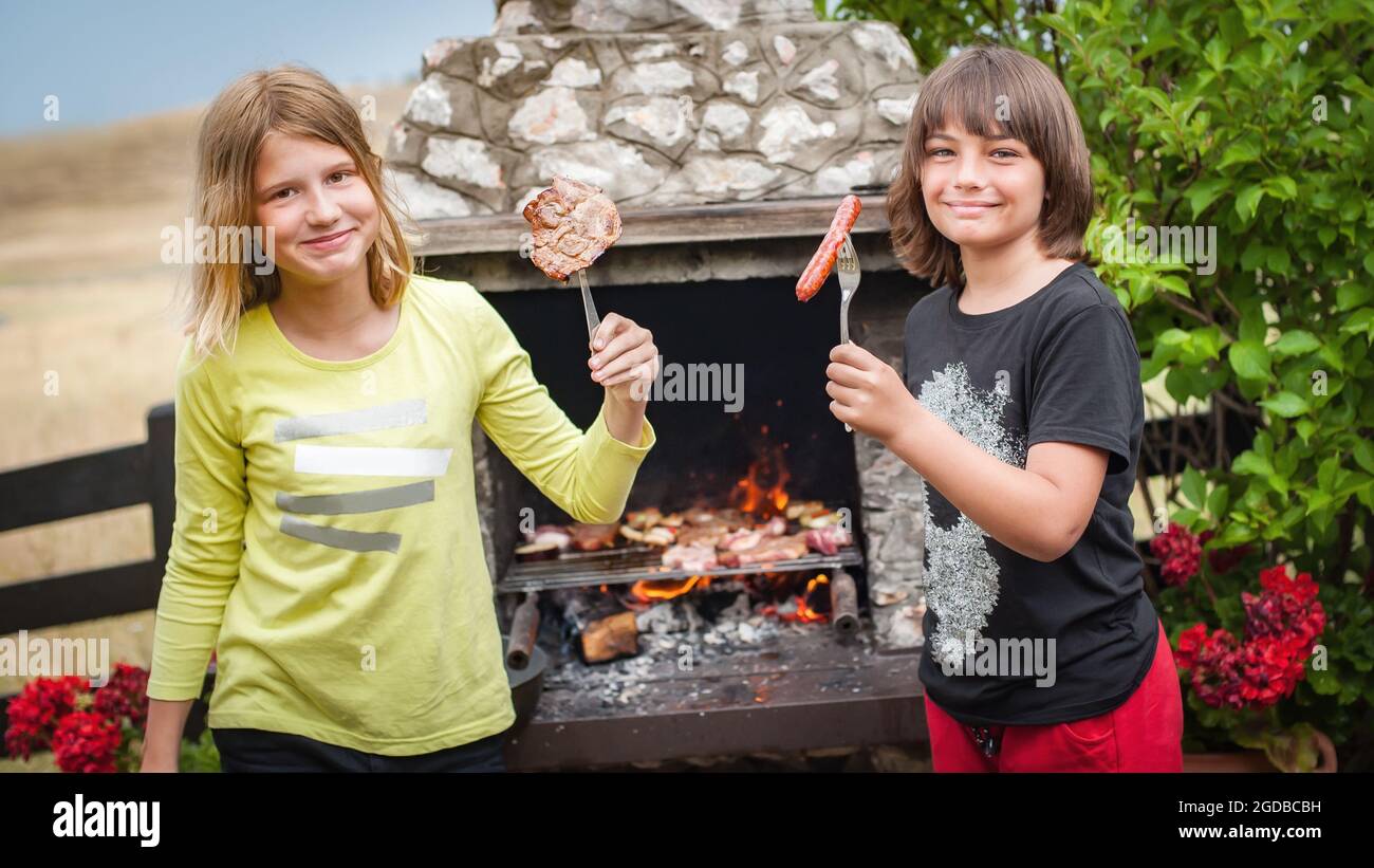 Children grilling meat. Boy and girl making barbecue on the grill on ...