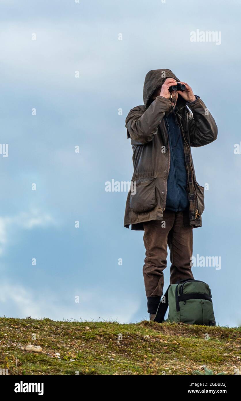man birdwatching standing on the beach looking through a pair of ...