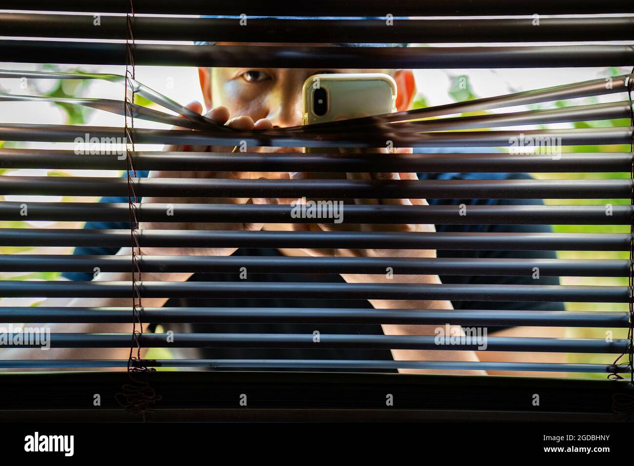 Man looking inside from the window and holding his smartphone to take a ...