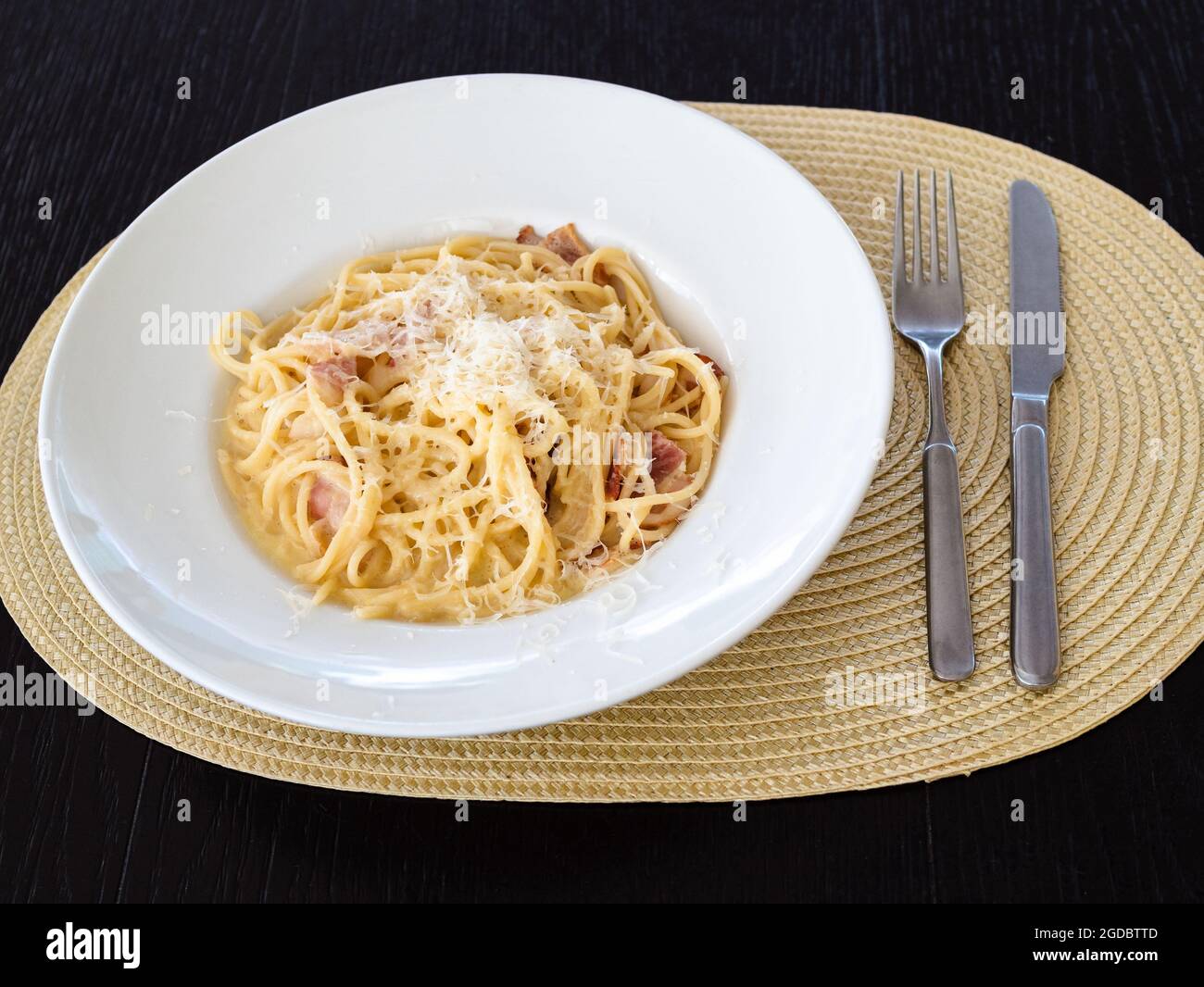 served spaghetti carbonara in white plate on straw mat on dark wooden ...