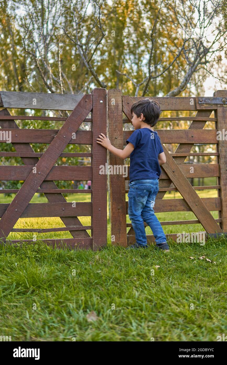 latin kid wearing casual dress opening a wooden gate in the forest in ...