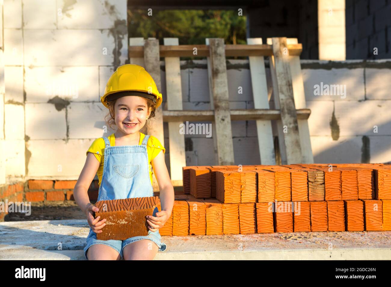 Little girl in a yellow hardhat is playing builder on the construction ...