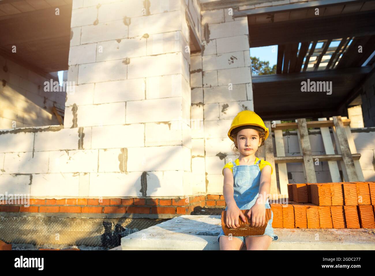 Little girl in a yellow hardhat is playing builder on the construction ...