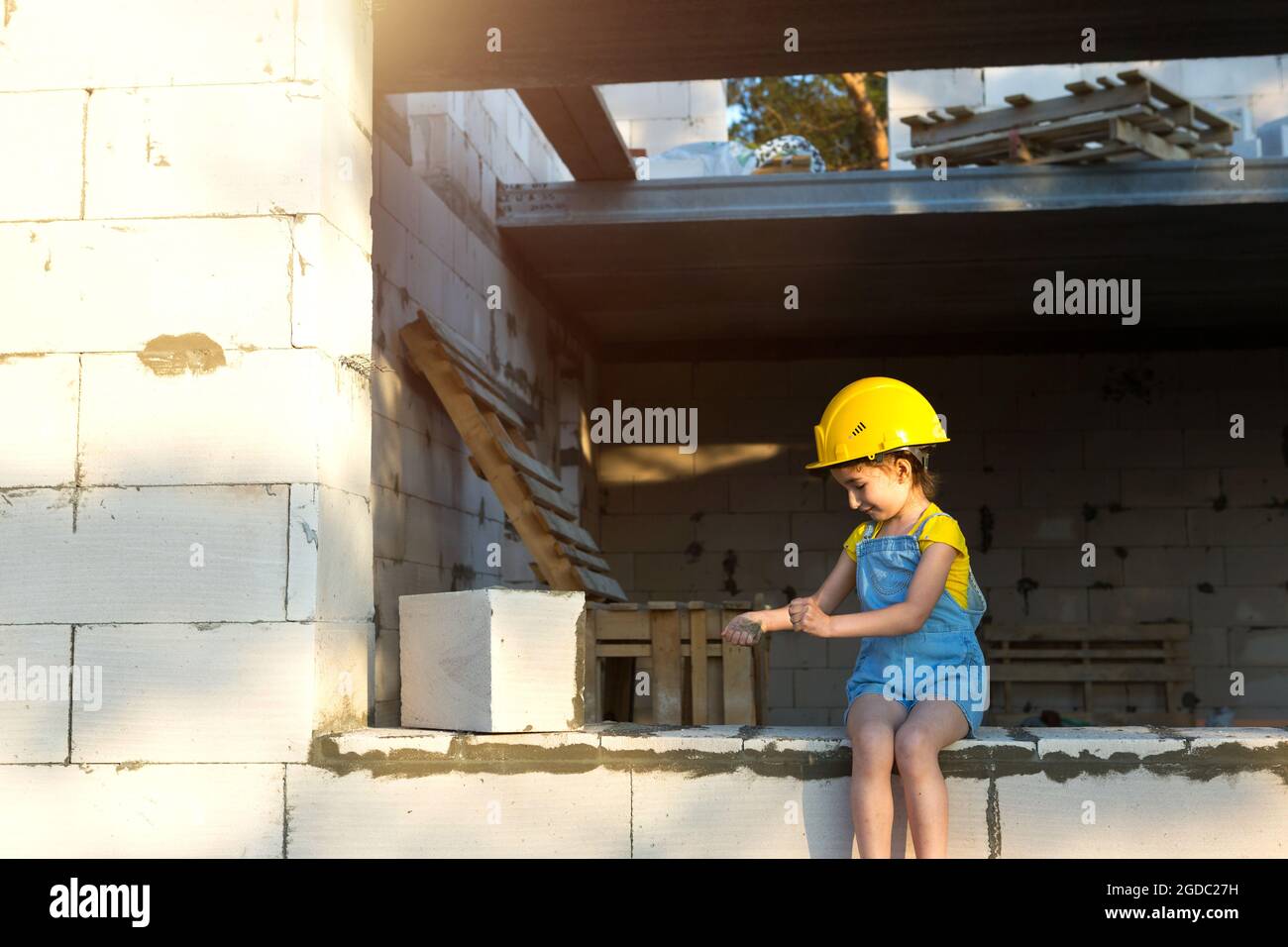 Little girl in a yellow hardhat is playing builder on the construction ...