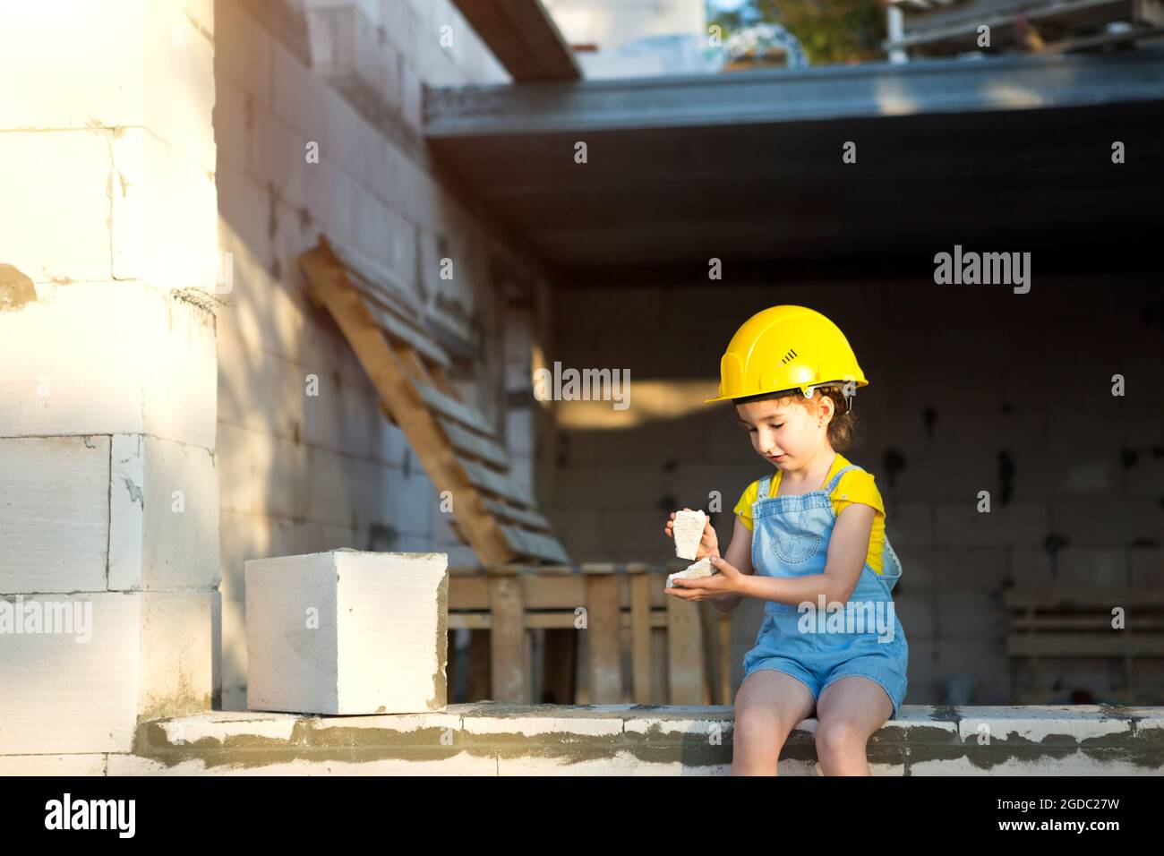 Little girl in a yellow hardhat is playing builder on the construction ...