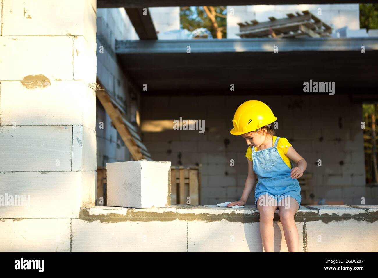 Little girl in a yellow hardhat is playing builder on the construction ...