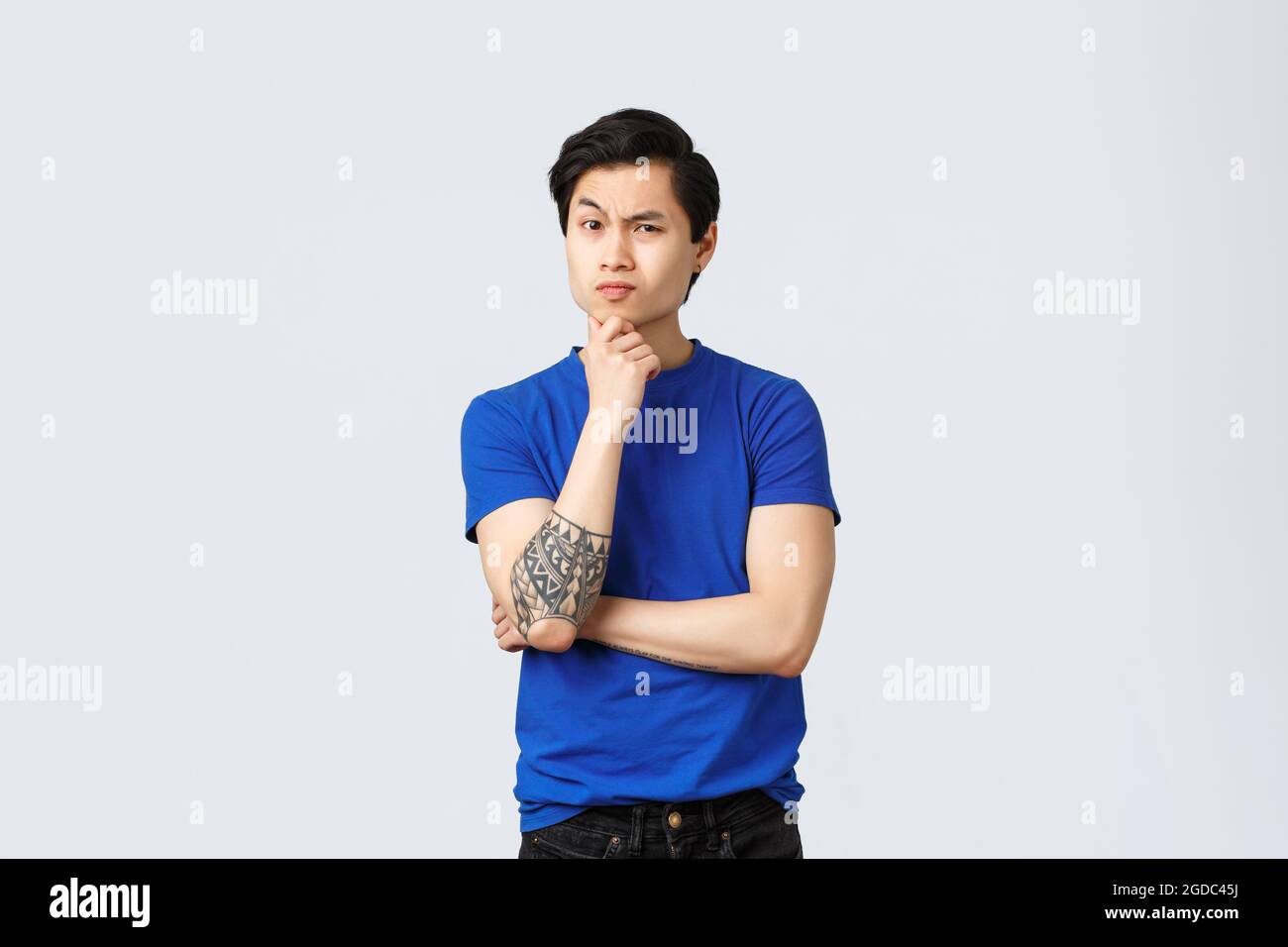 Skeptical, serious-looking asian man in blue t-shirt with tattoos ...