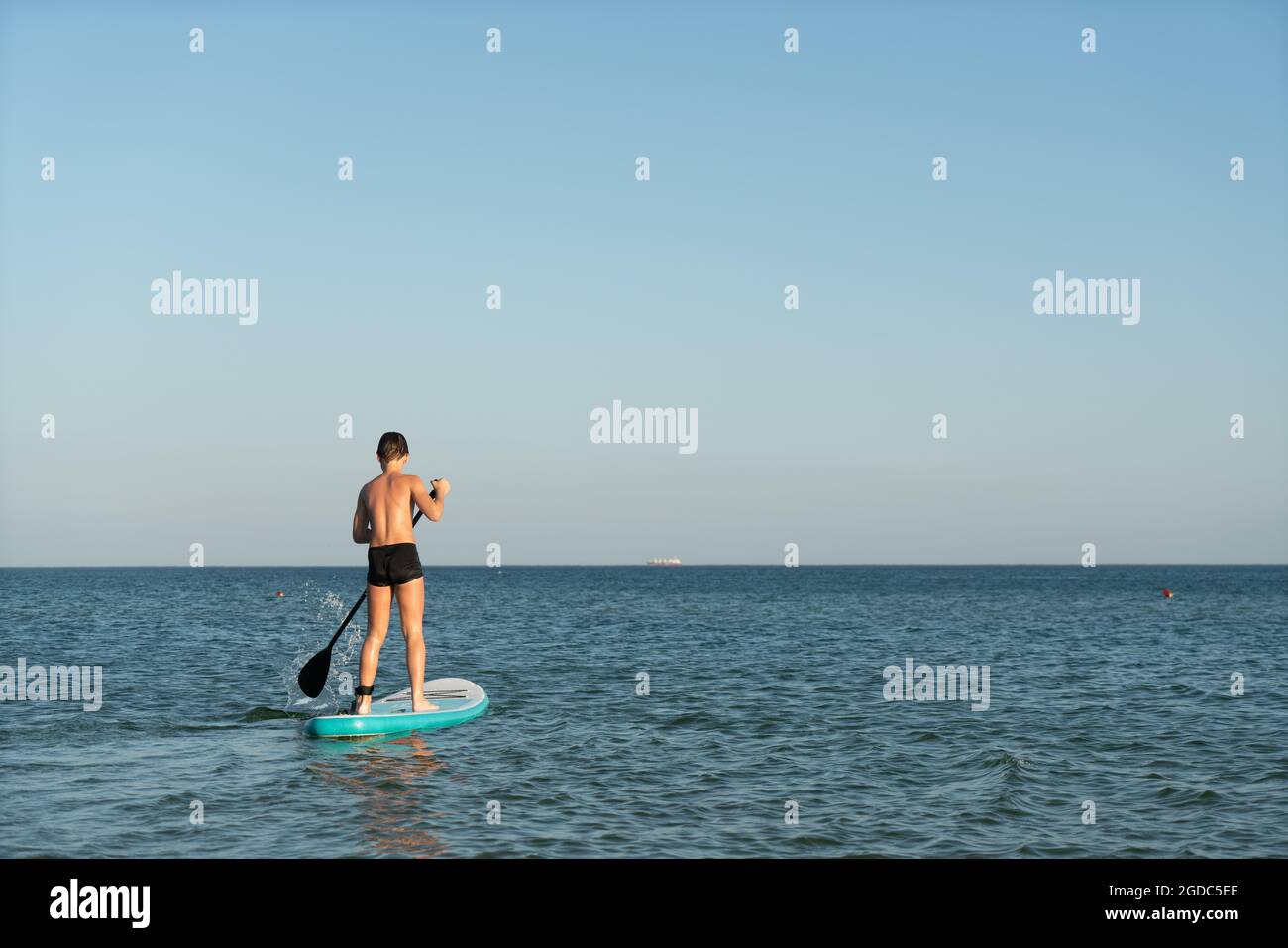 A 12 year old boy learns to stand on a SUP board in the sea near the ...