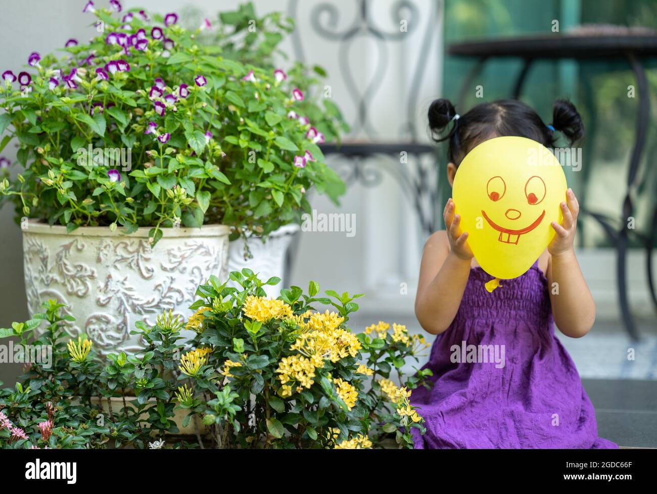 Cute little girl holding a yellow balloon with a happy face in front of ...
