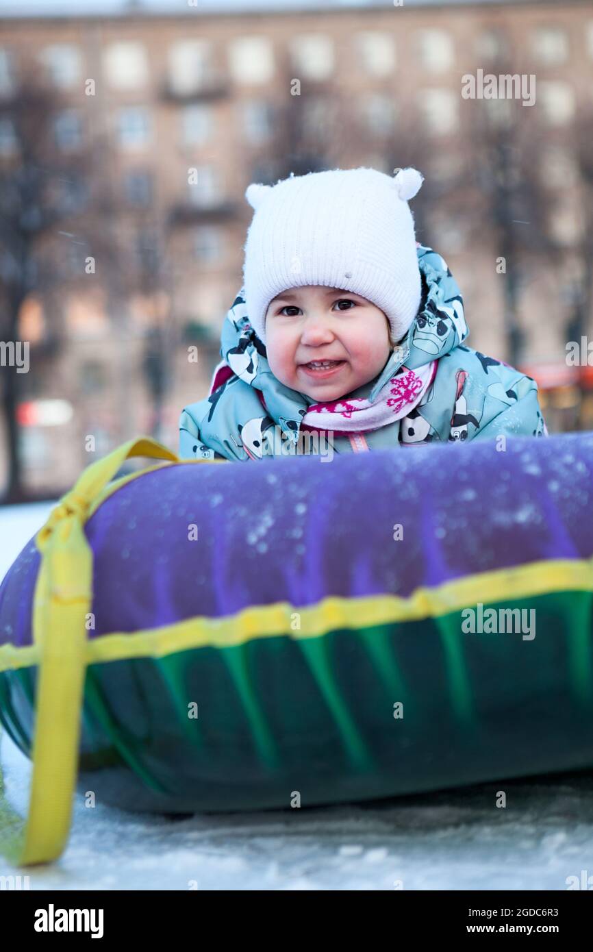 Smiling and happy baby with snowing tube, sliding on snowy slope ...