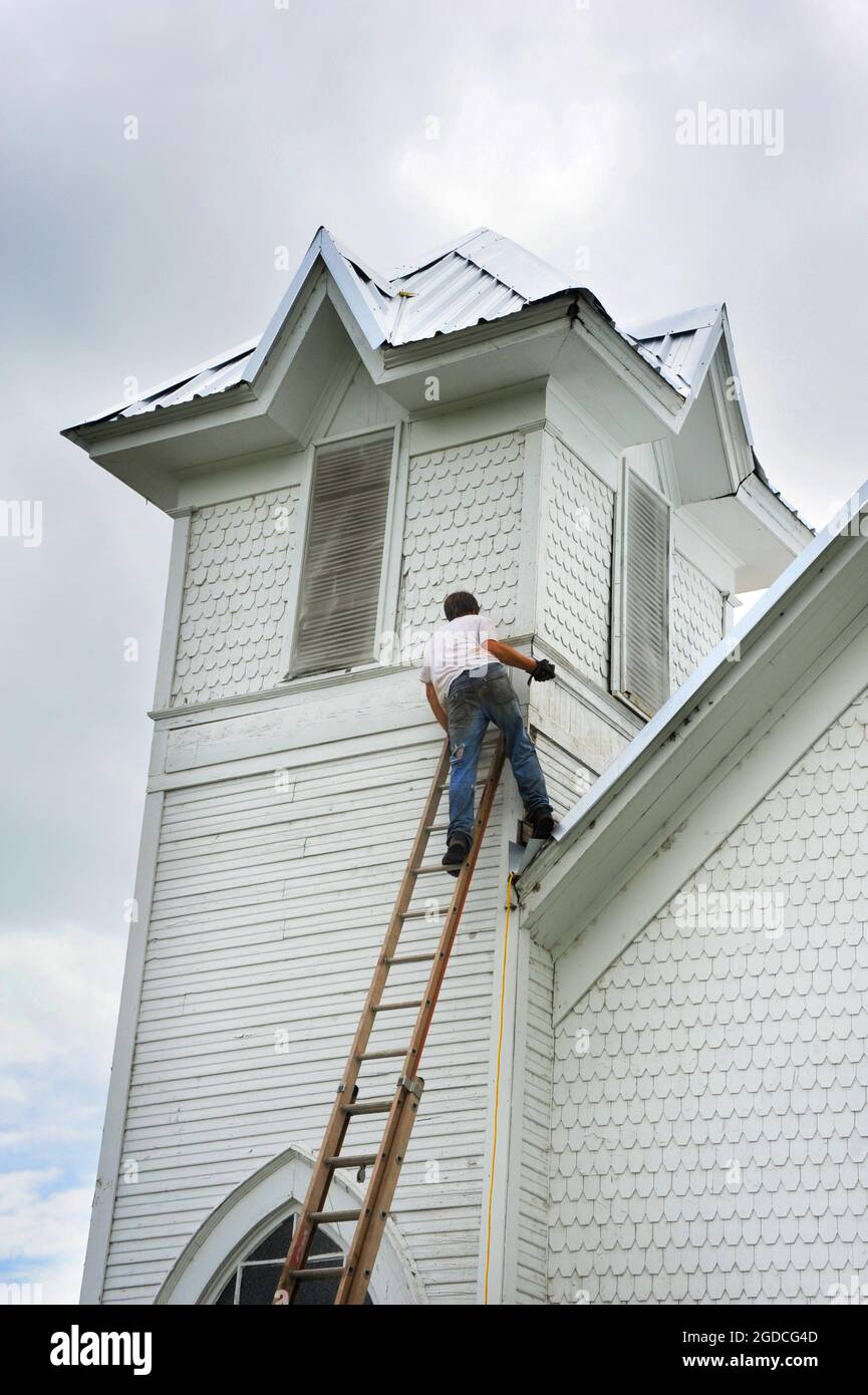 Young man balances on a ladder leaning against a church in Northern ...