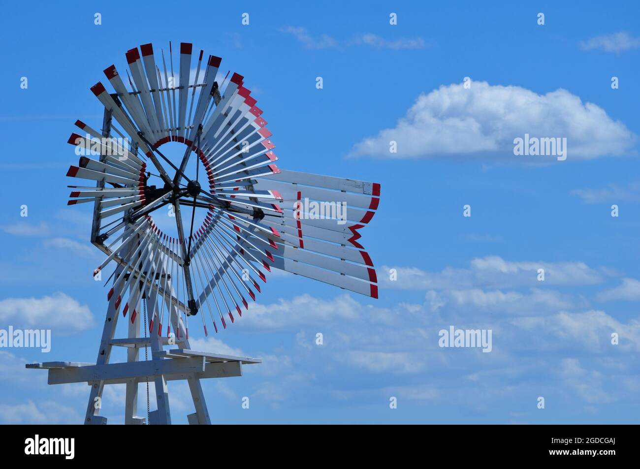 Unusual wildmill is metal with red tipped blades. Blue sky and clouds ...