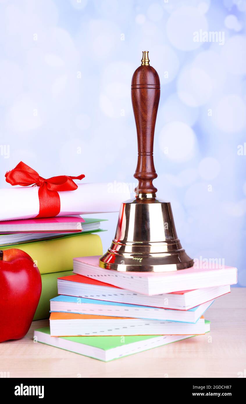 Gold school bell with school supplies on table on bright background ...
