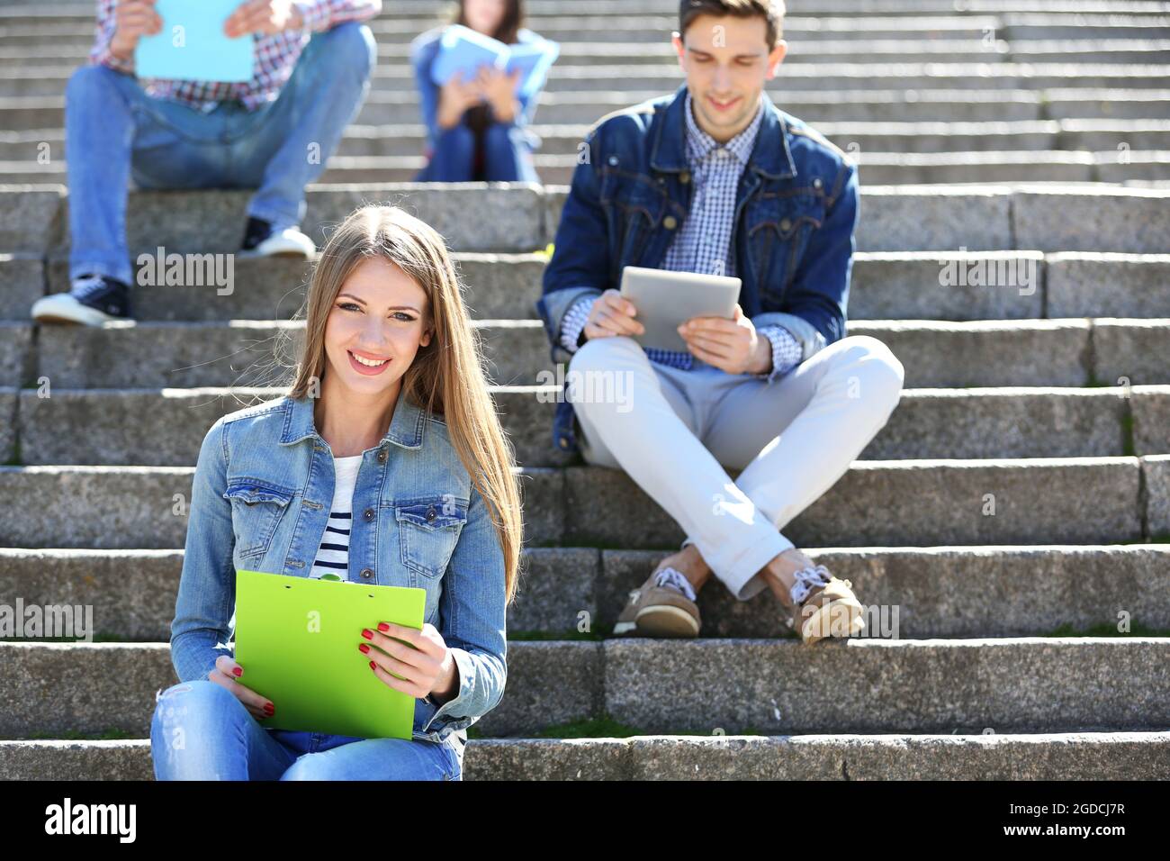 Happy students sitting on stairs in park Stock Photo - Alamy